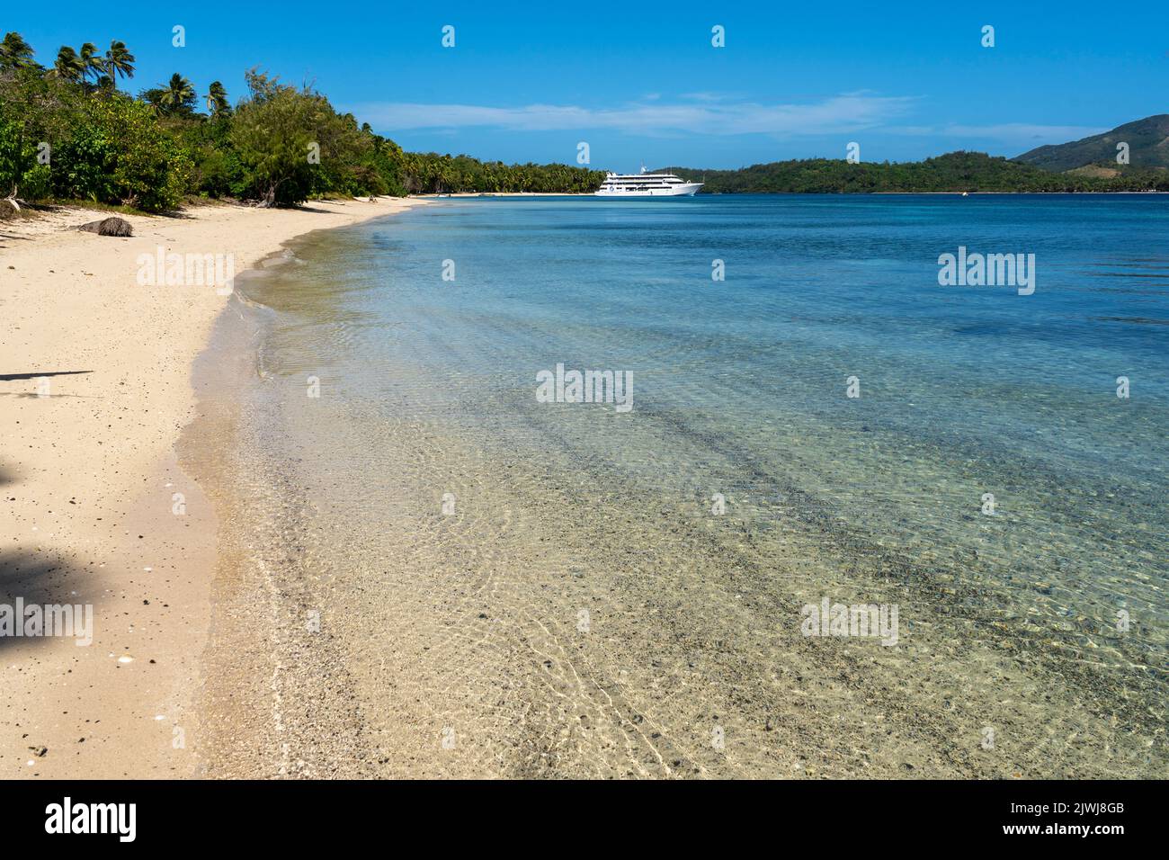 Cruise ship anchored in Blue Lagoon off tropical beach with clear blue ...