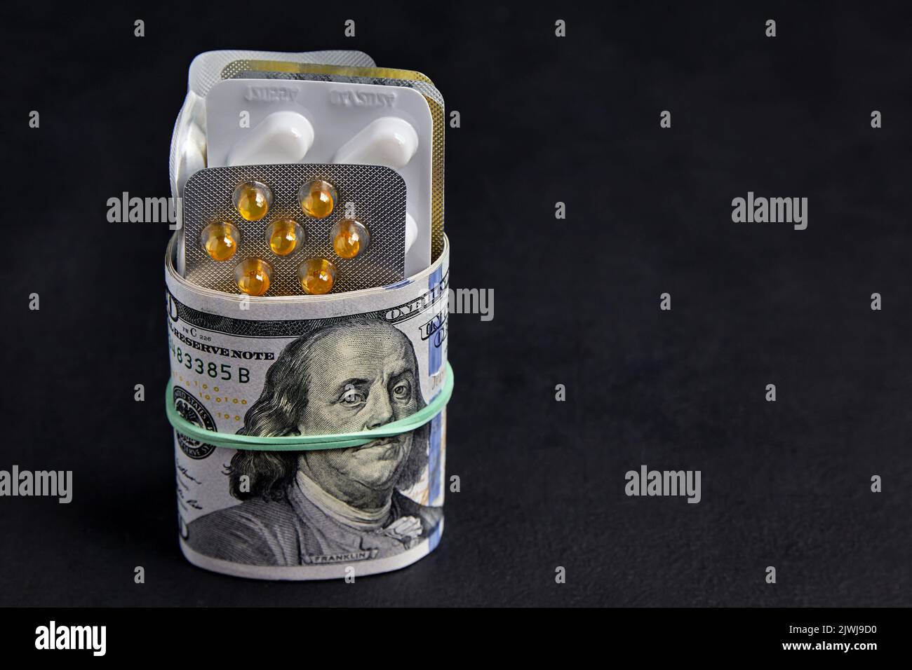 Pills and tablets in a blister pack are wrapped in dollar bills held ...