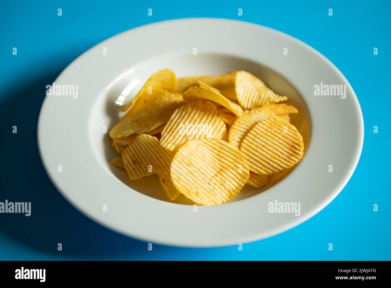 Potato chips served in dish on blue background Stock Photo - Alamy