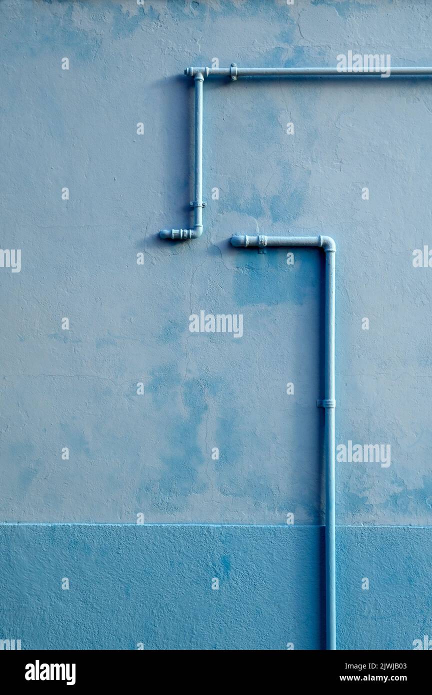 Thin pipelines attached to light blue stucco wall of building on town ...