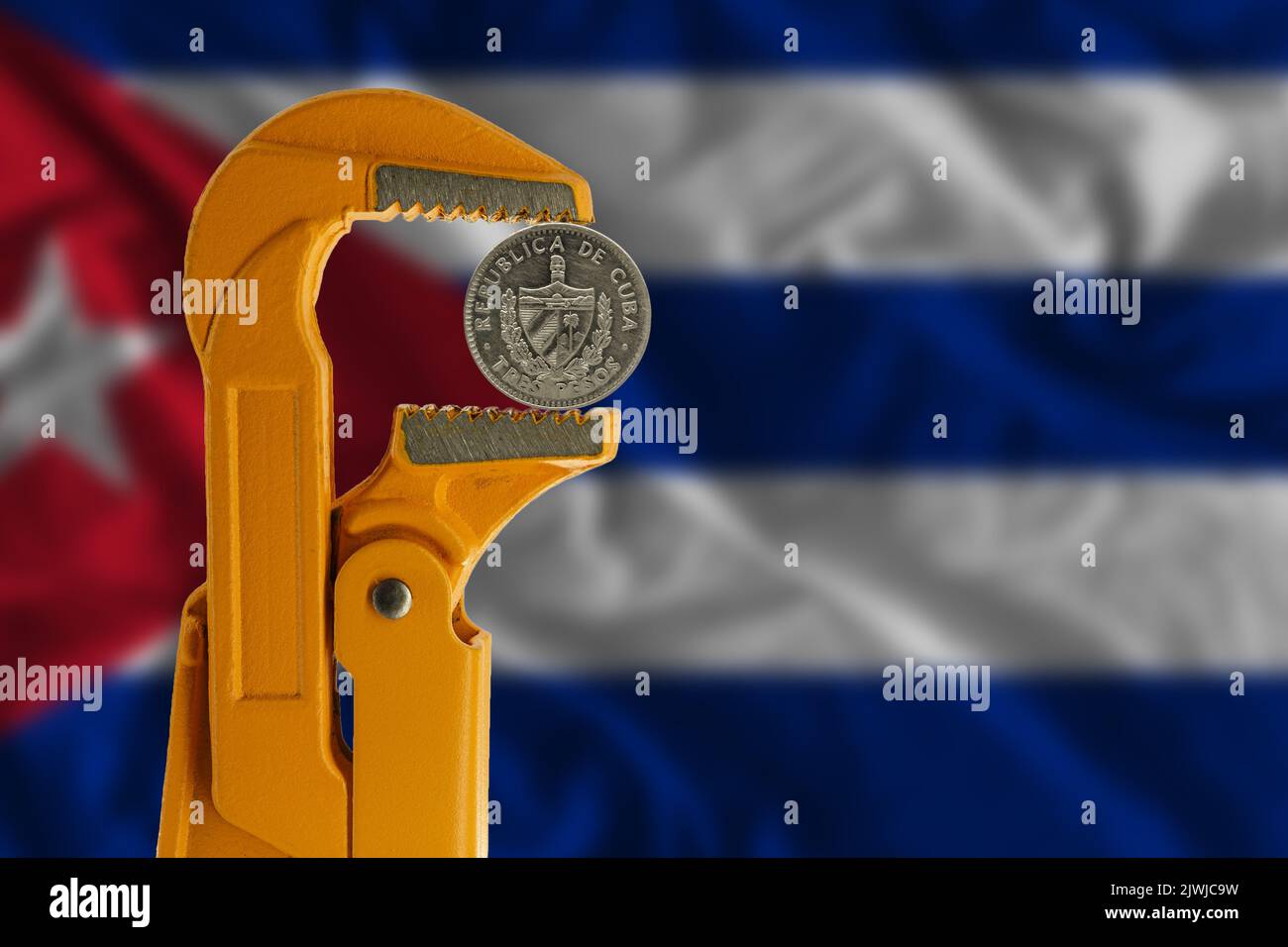 Three Cuban pesos coin held in an orange plumber wrench against the ...