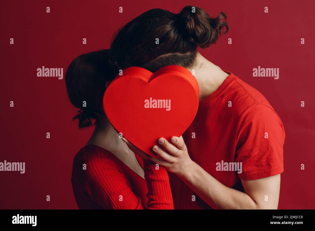 Man and woman young couple kissing and hiding behind heart-shaped box ...