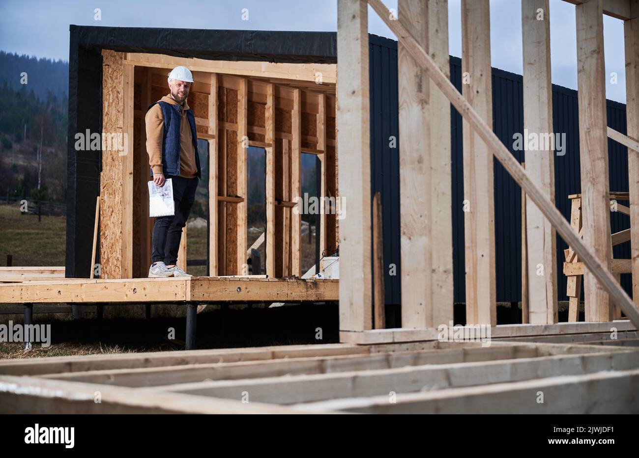 Male inspector building wooden frame house on pile foundation. Man builder standing on ...