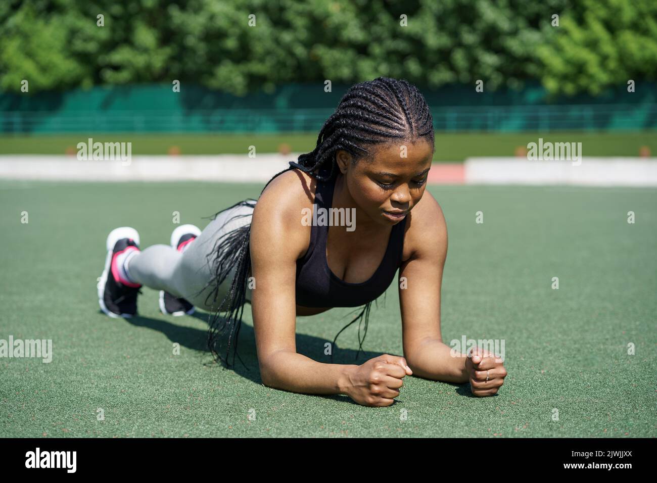 African American woman with long braids does plank exercise on green ...
