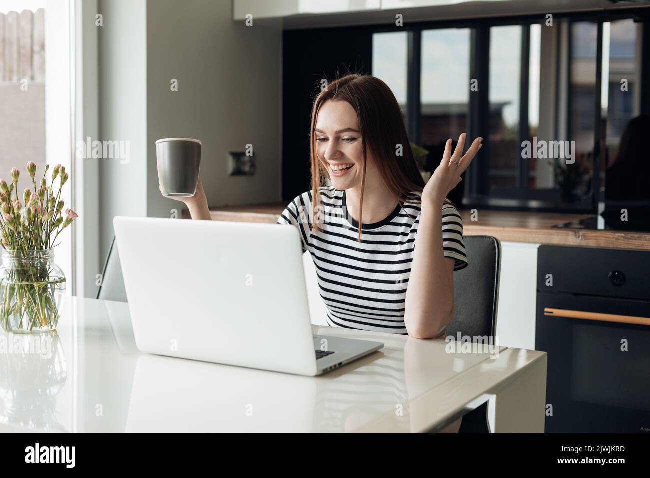 Young laughing and cheerful female using white laptop and drinking ...