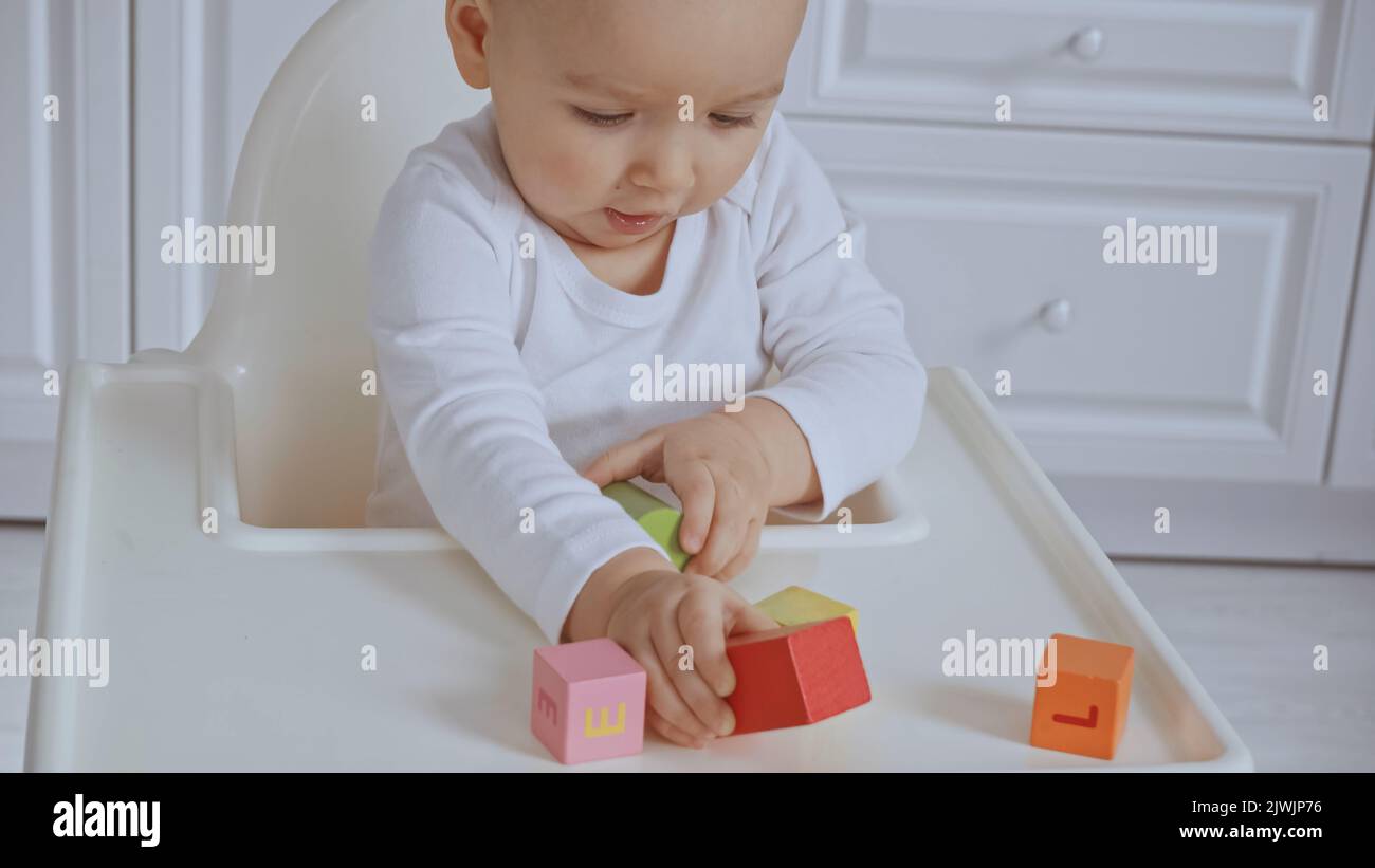 focused baby girl sitting in feeding chair and playing with wooden ...