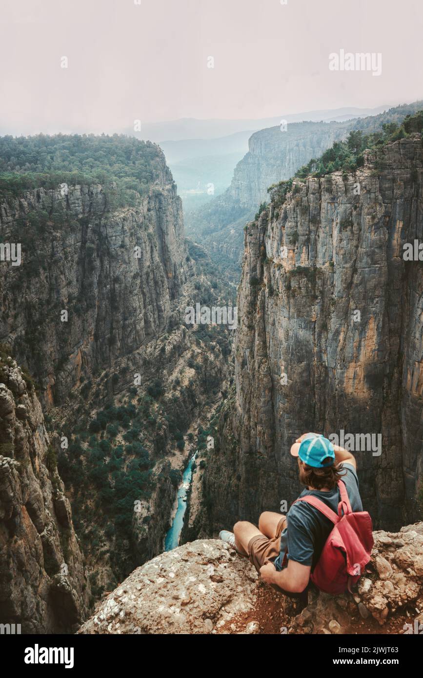 Man traveler sitting alone on cliff edge hiking with backpack travel ...