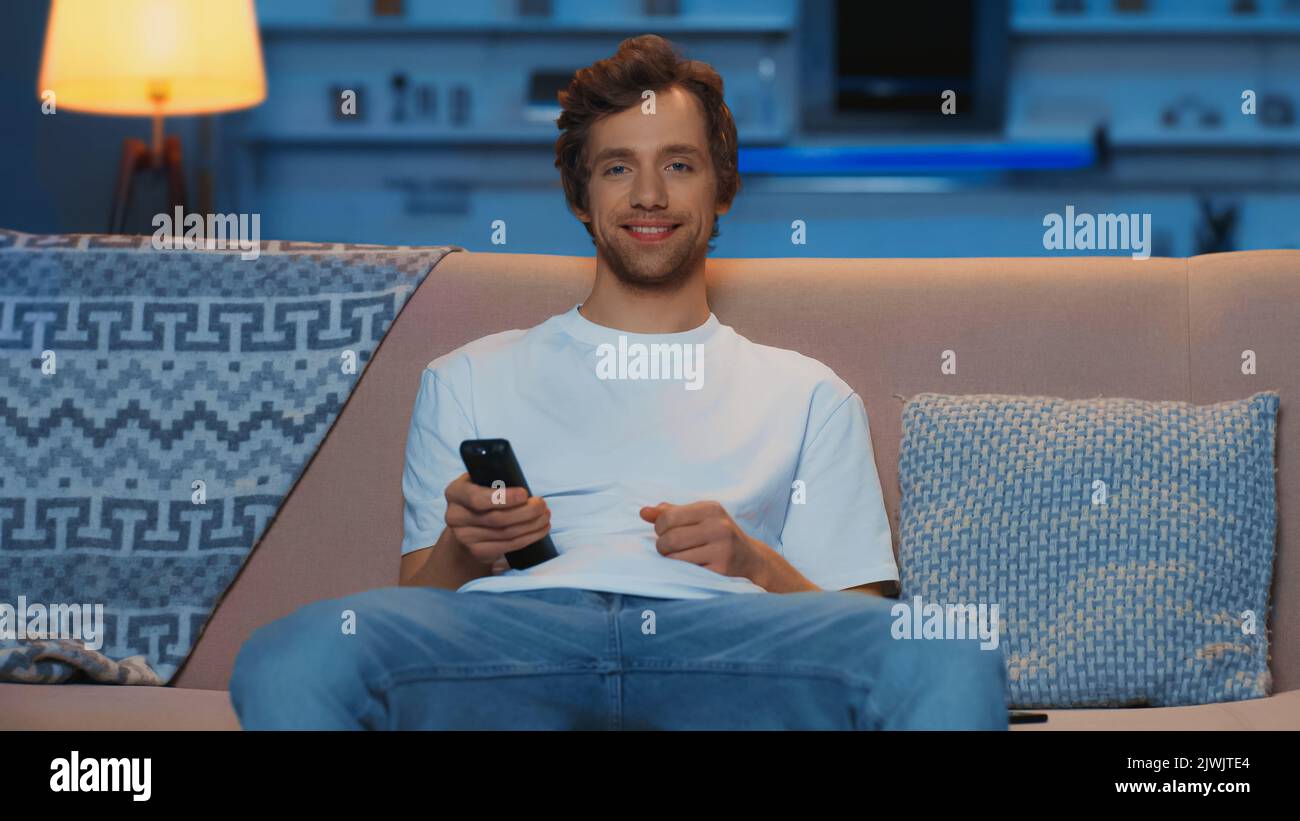 happy young man using remote controller while watching tv on couch ...