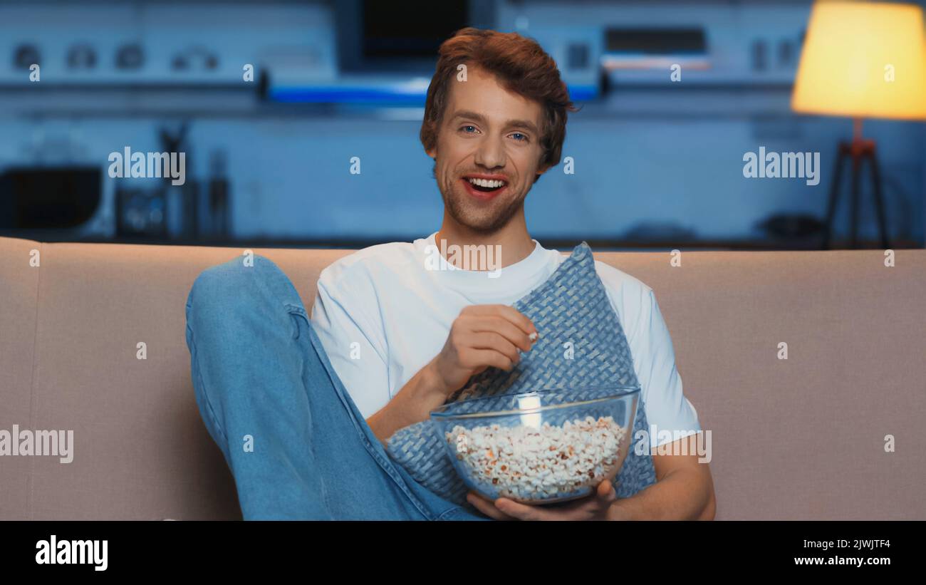 happy young man eating popcorn while watching movie in living room ...