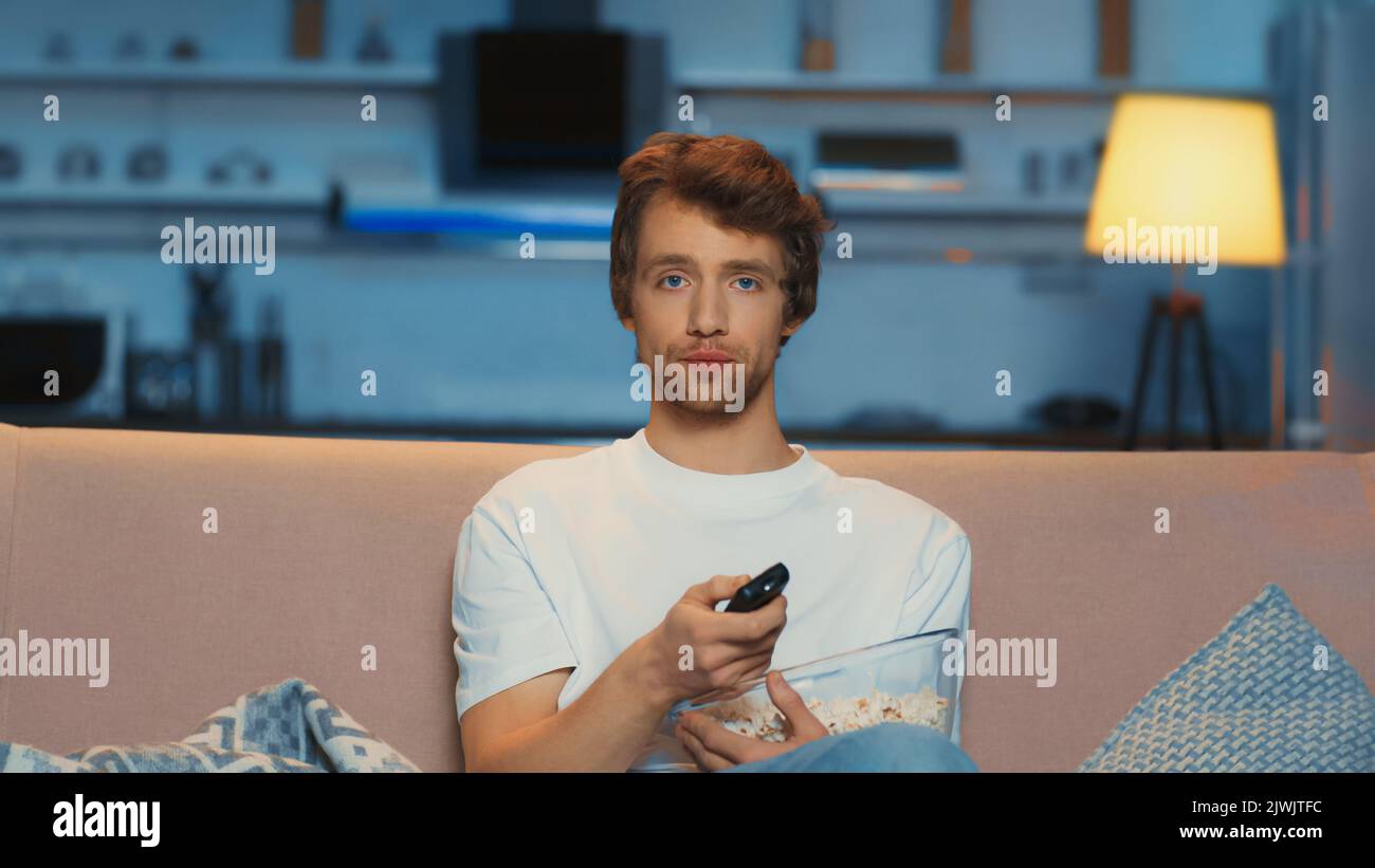 young man holding remote controller while clicking channels and ...