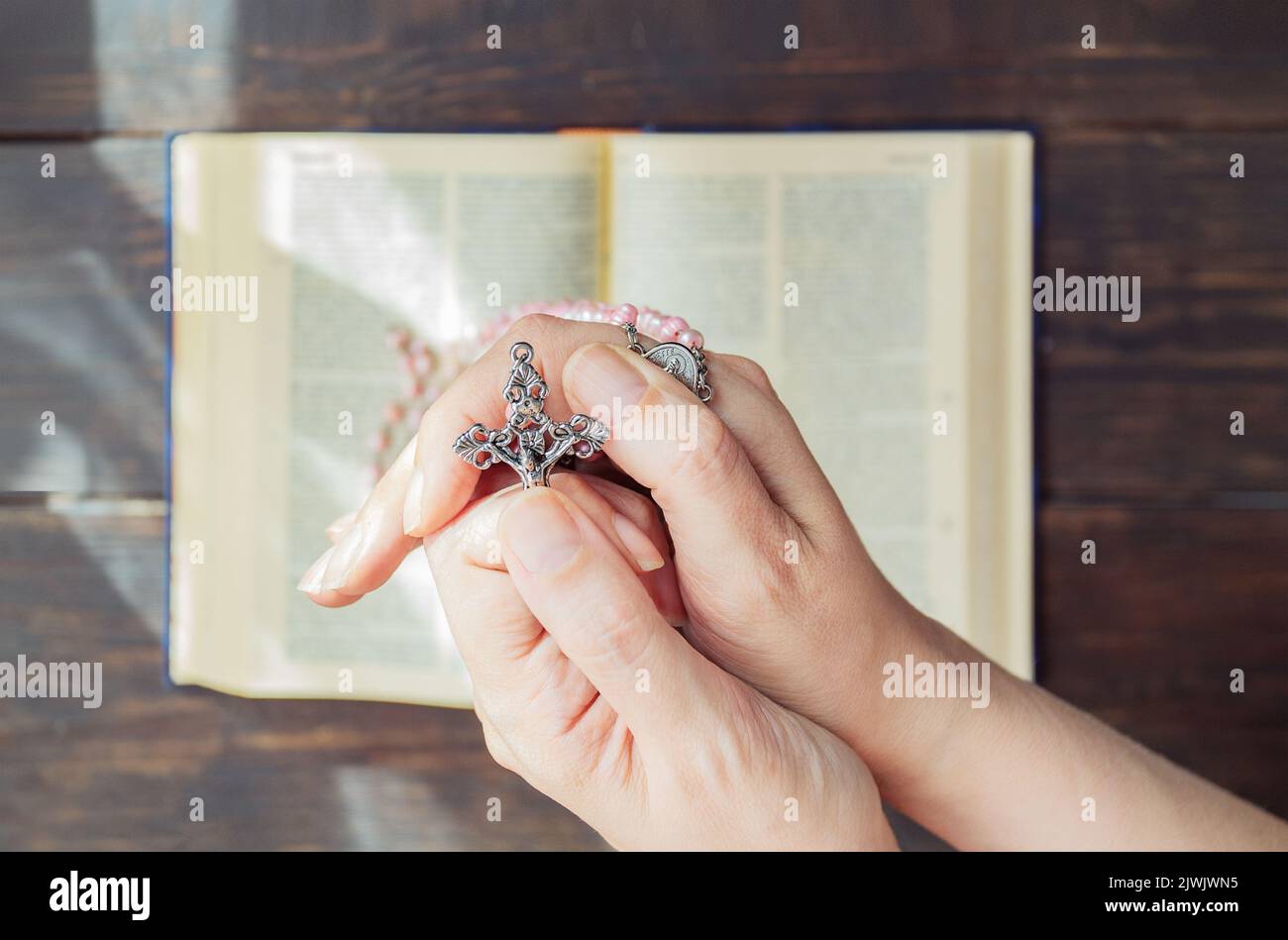 Hands folded in prayer with cross rosary on a Holy Bible background ...
