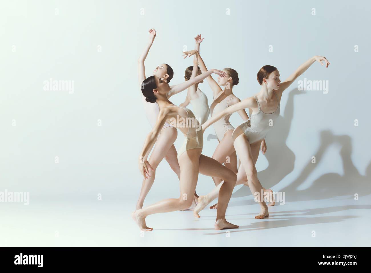 Group of young women, ballerinas dancing, performing isolated over grey ...