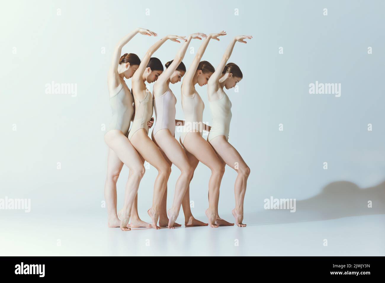 Group of young girls, ballet dancers performing, standing together closely with raised hands ...