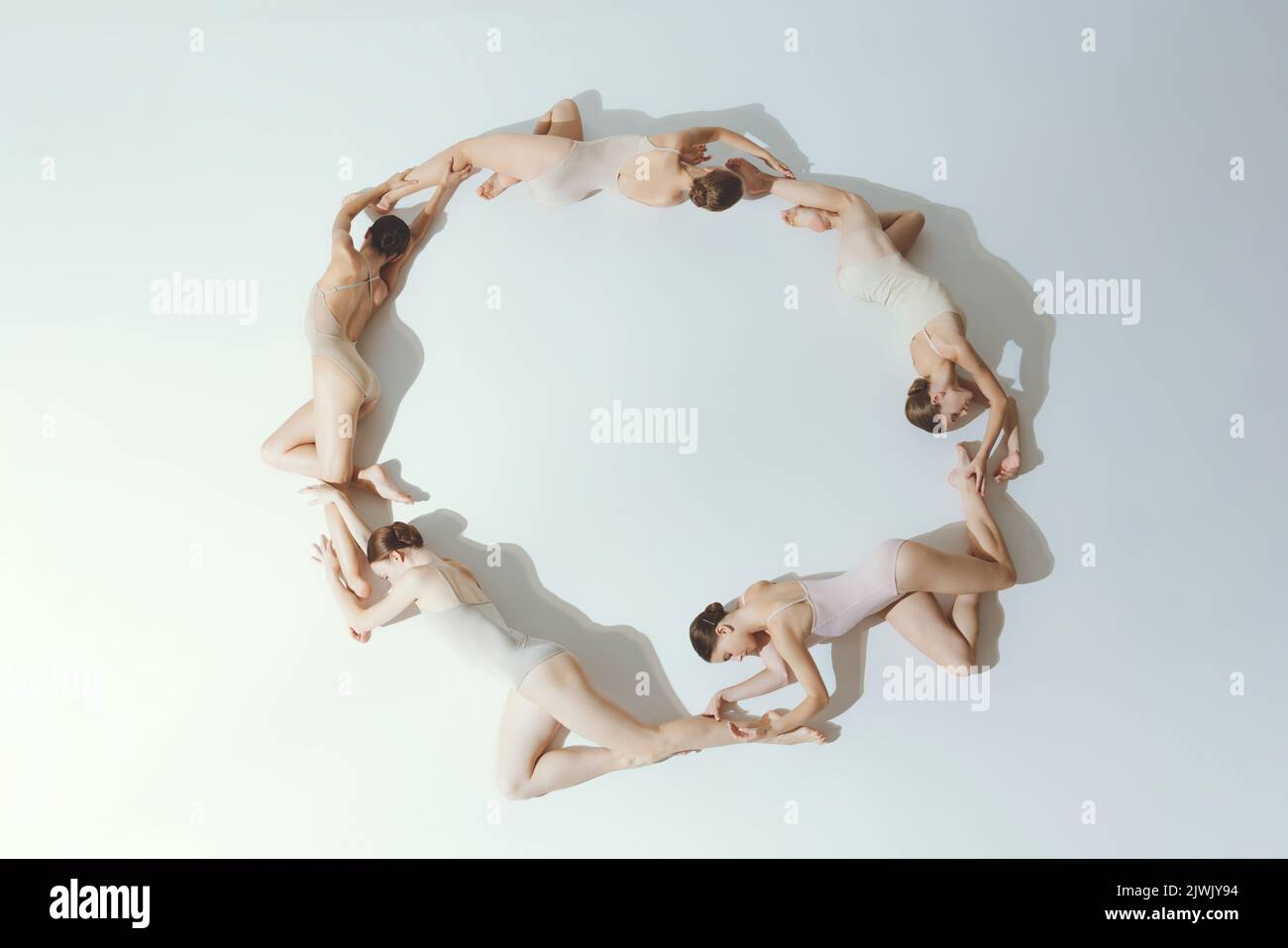Group of young girls, ballet dancers performing, posing on floor isolated over grey studio ...