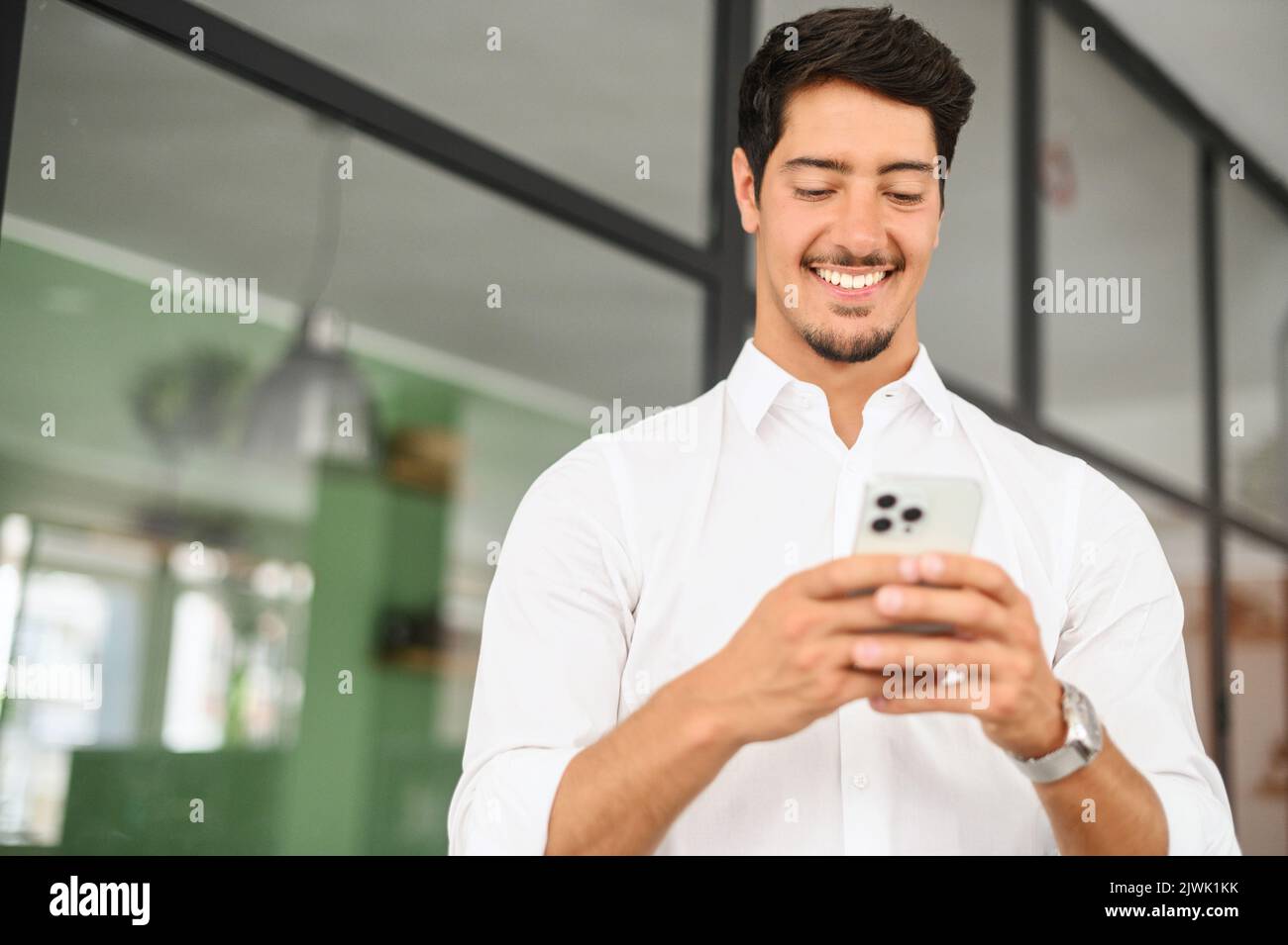 Positive hispanic male employee using smartphone for online communication, smiling businessman ...