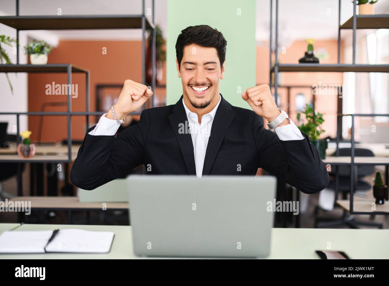Happy excited hispanic office worker sitting at desk in front of laptop ...