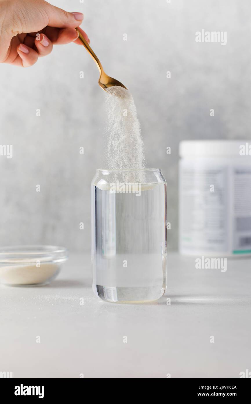 Collagen powder is poured into a glass of water from a golden spoon on ...