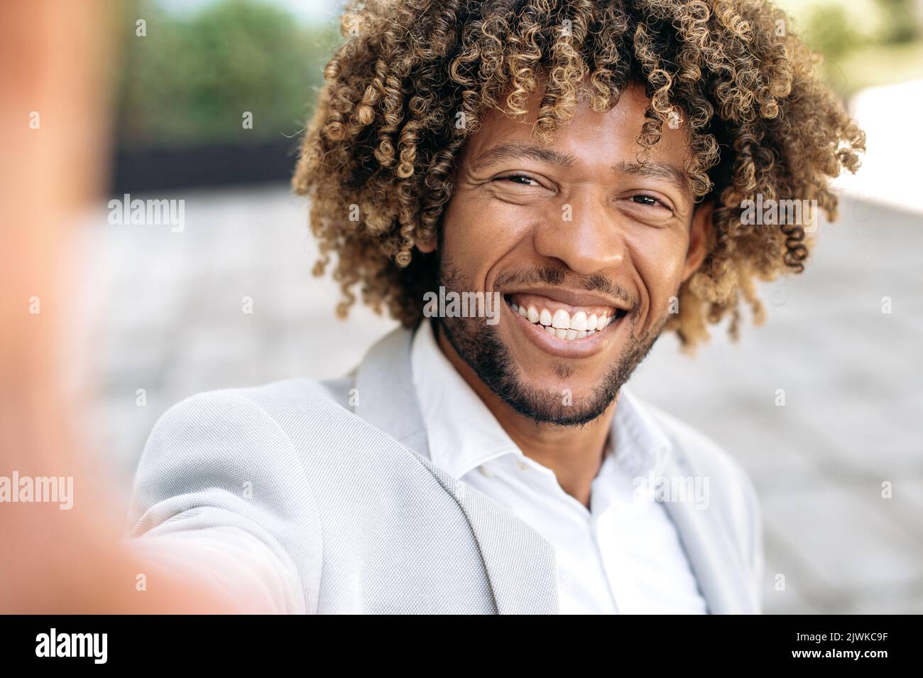 Cheerful handsome curly haired mixed race man standing outdoors, taking ...