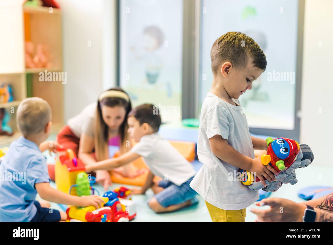 Toddlers boys and their nursery teacher playing with plastic toys and ...