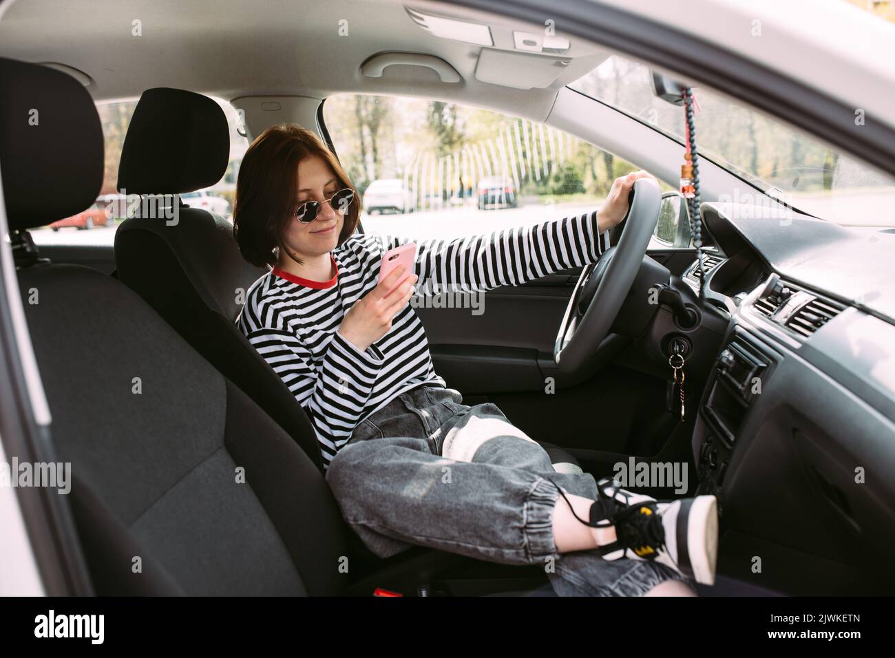 Portrait of a young brunette woman driving in a car using a smartphone ...