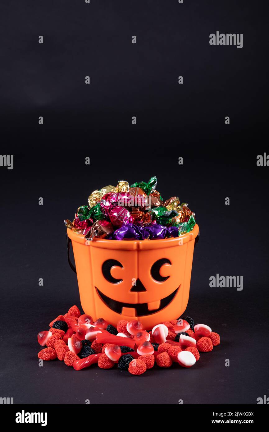 Halloween pumpkin shaped bucket full of candies against black ...