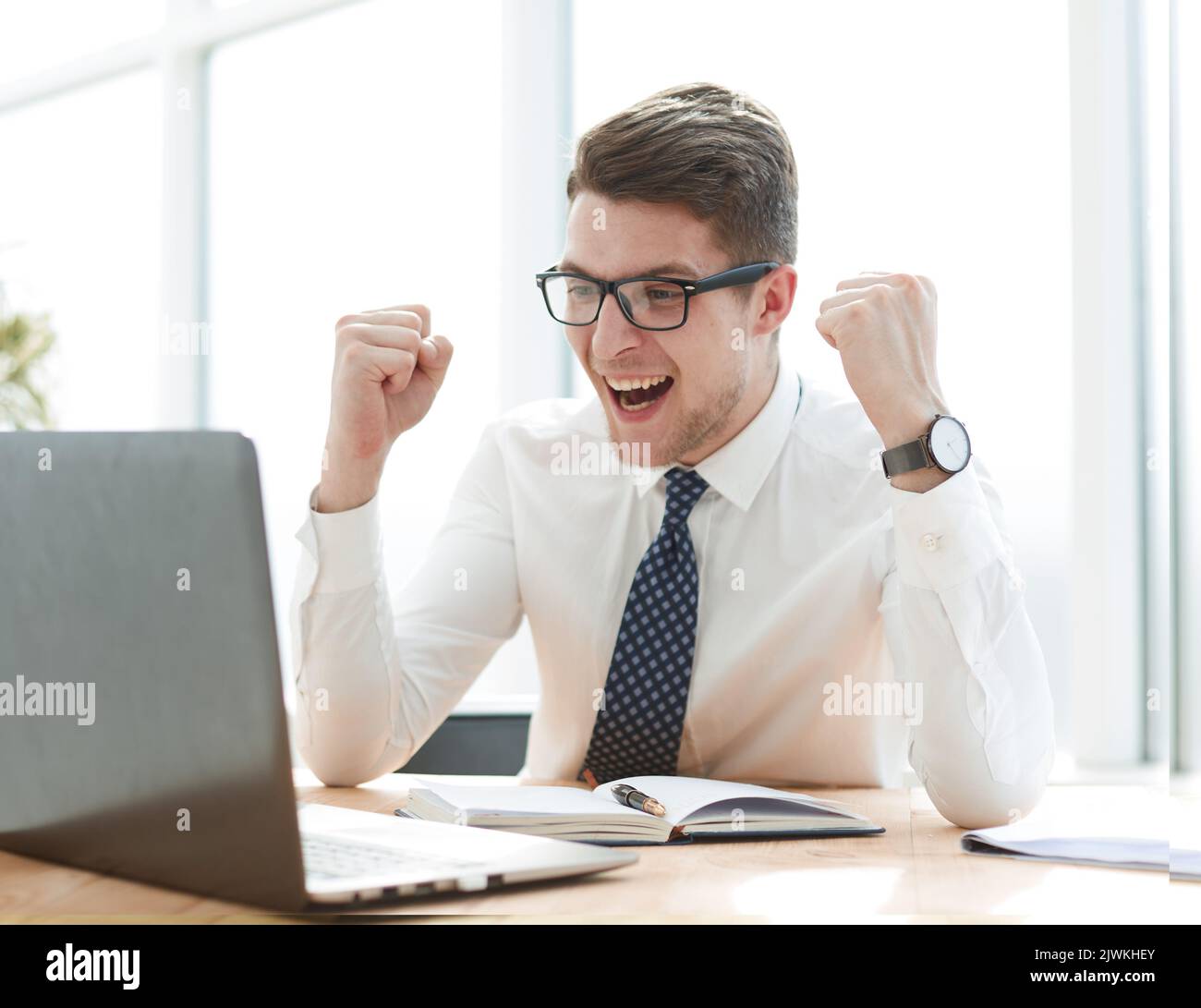 Happy young businessman raising hands in front of laptop at office desk ...