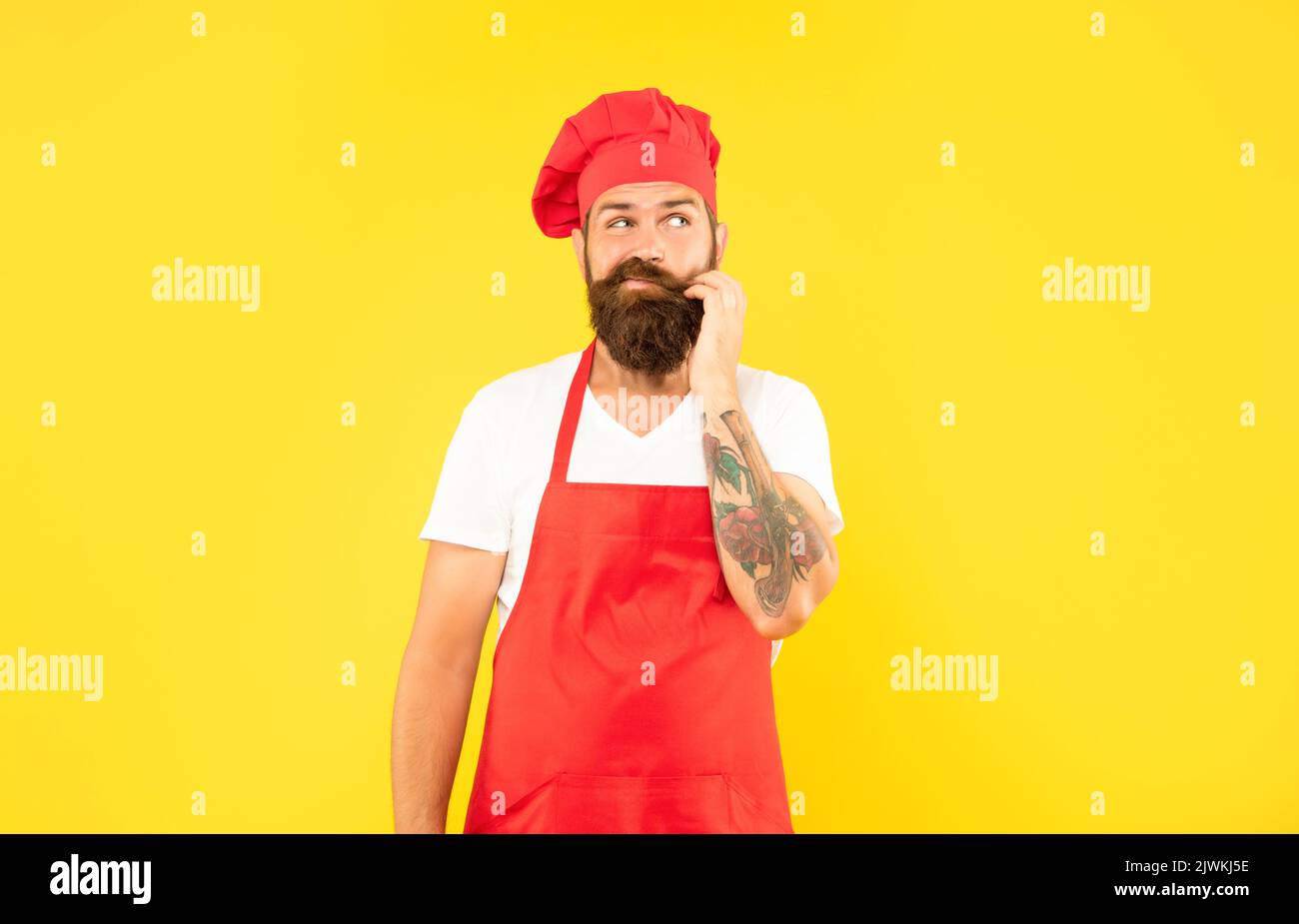 Hesitant man in red toque and apron stroking chin yellow background ...