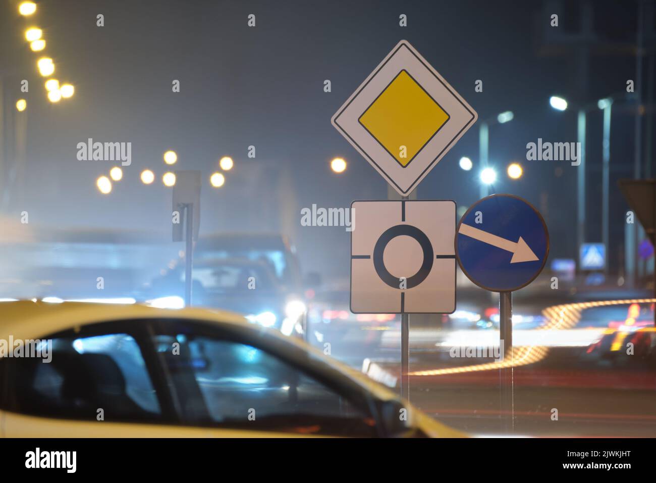 Roundabout road signs with blurred cars on city street traffic at night ...