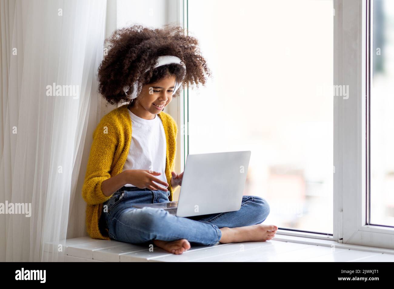 Cheerful little black girl with wireless headset using laptop Stock ...