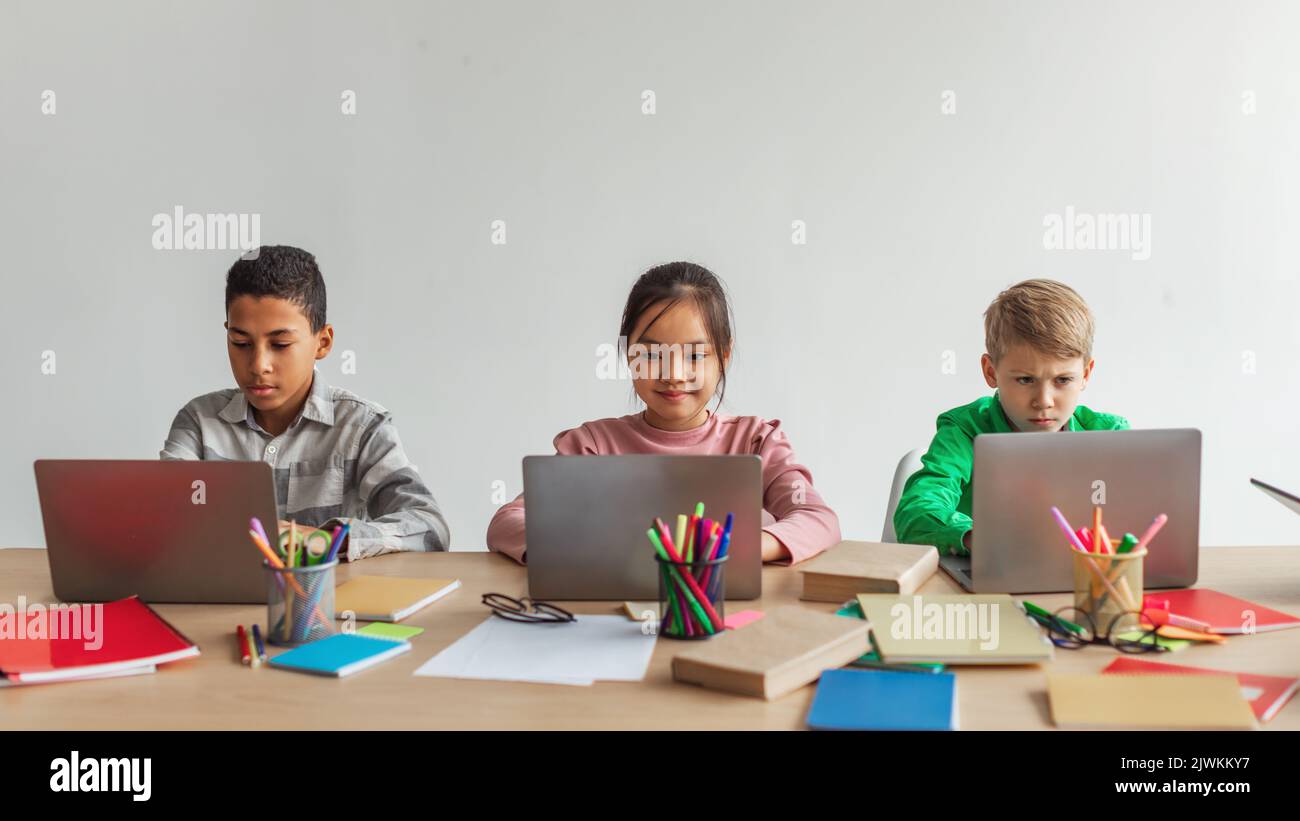 Three Multiracial School Kids Using Laptops Learning Online At School ...