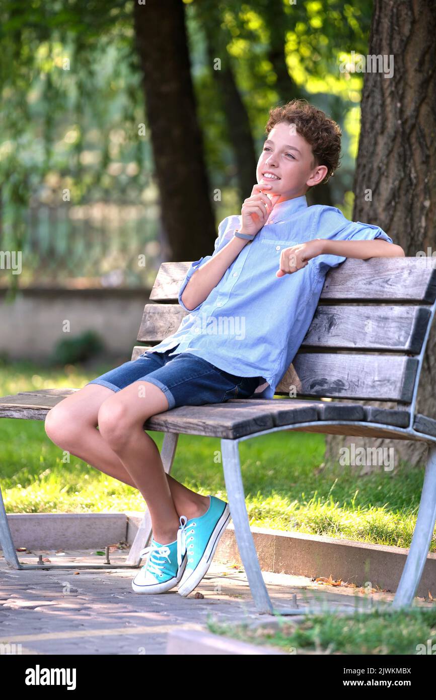 Young happy child boy relaxing sitting on bench in summer park ...