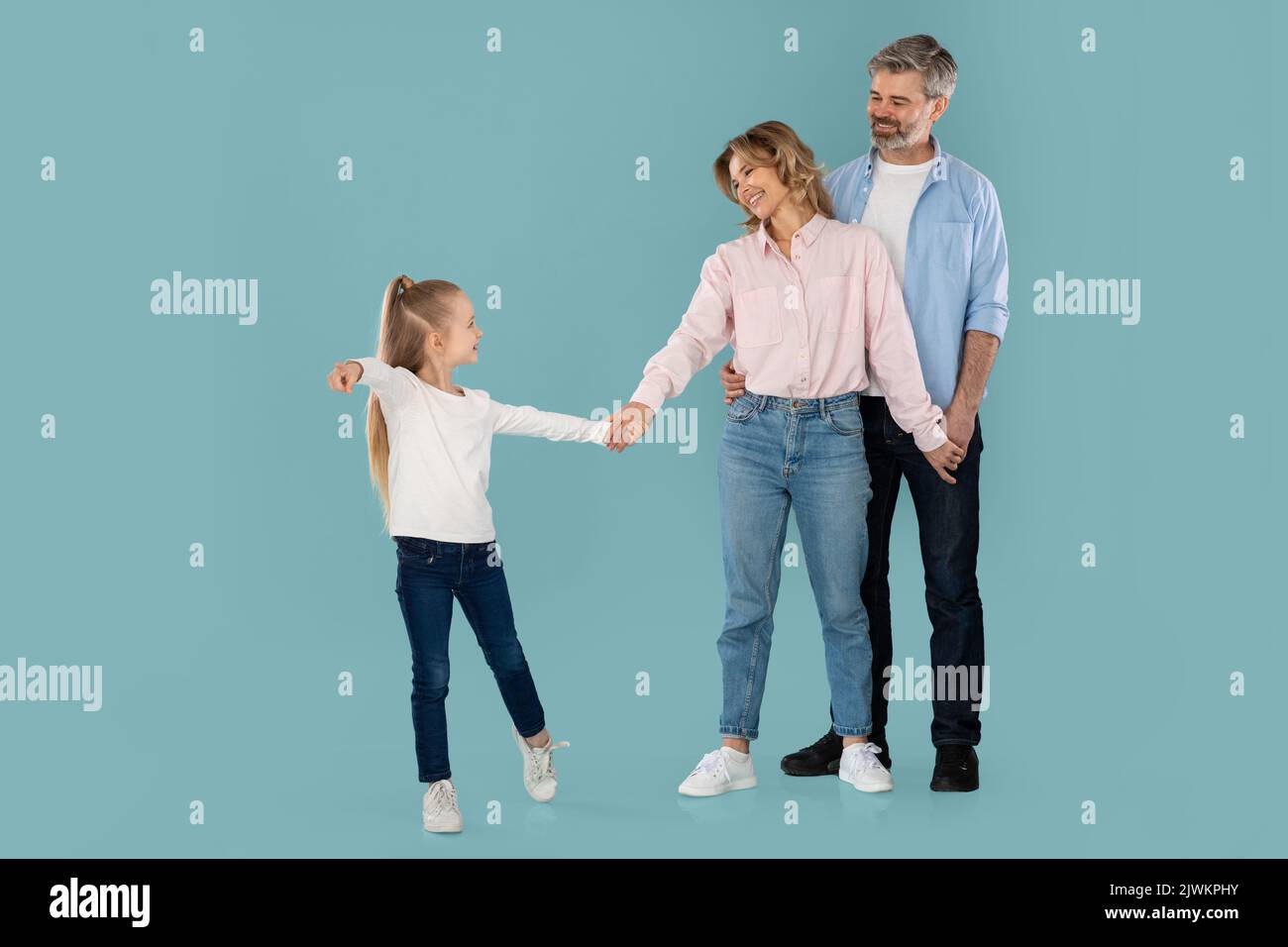 Daughter Pointing Finger At Camera Holding Hands With Parents, Studio ...