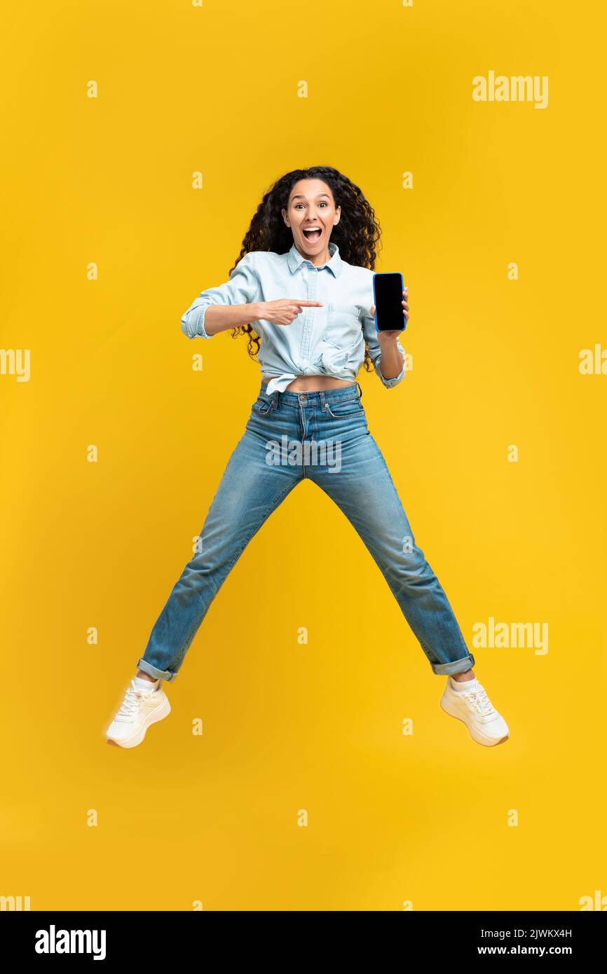 Excited lady pointing at smartphone with empty screen, jumping up in ...