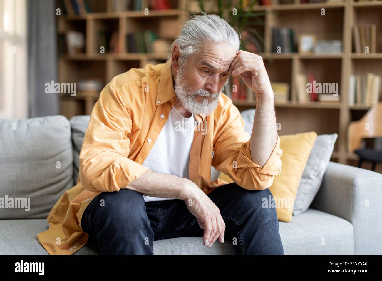 Upset old man sitting on couch alone, home interior Stock Photo - Alamy