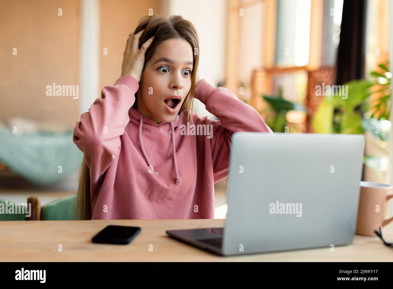 Shocked teenage girl looking at laptop and touching head, having ...
