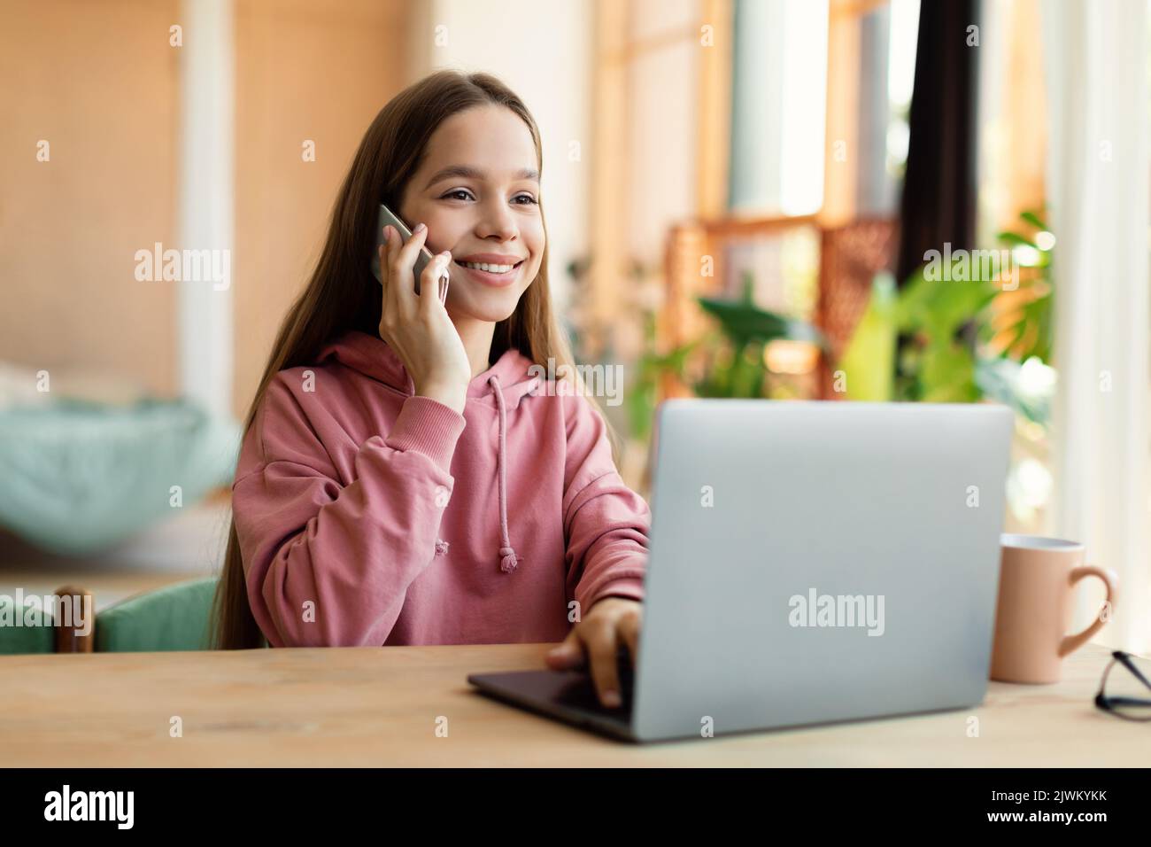 Happy teen girl talking on cellphone and typing on laptop computer ...