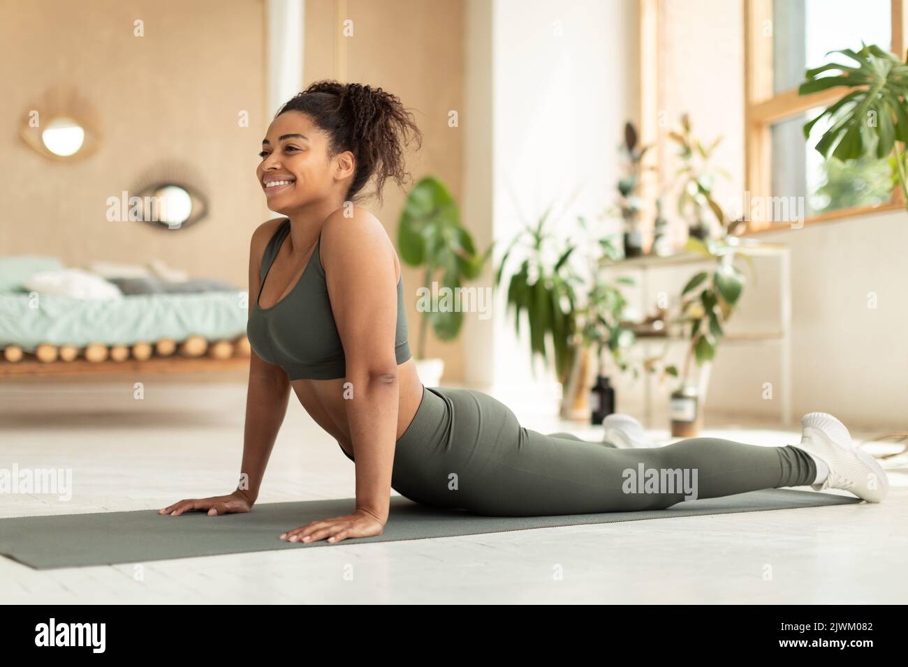 Smiling black lady practicing yoga, doing Ardha bhudjangasana, Sphinx ...