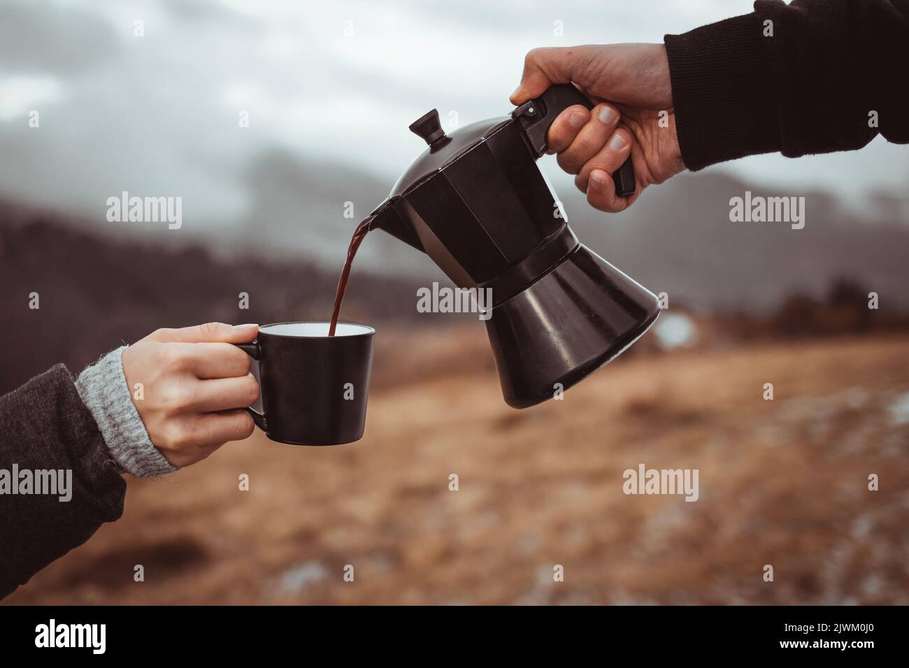 Person pouring out coffee from moka pot into cup outdoors with fog ...