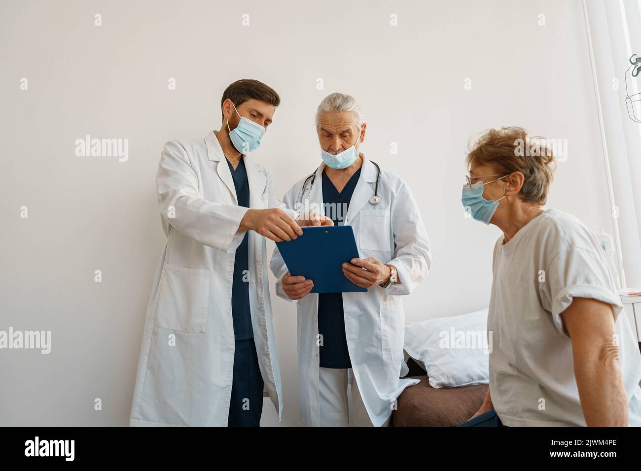 Doctors in masks explain to a sick patient in a wheelchair her ...