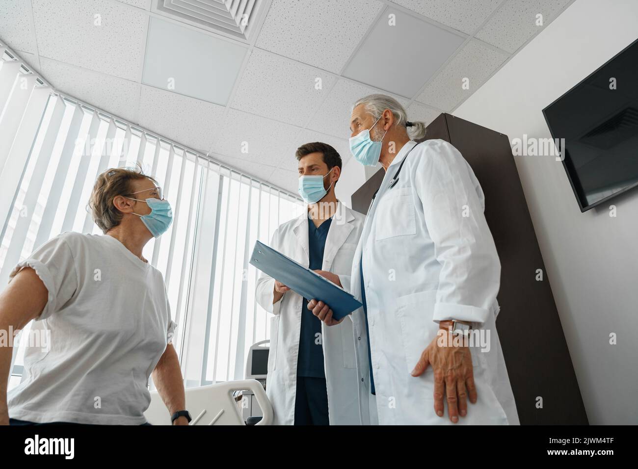 Doctors in masks explain to a sick patient in a wheelchair her ...