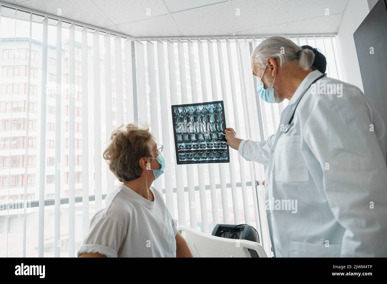 Doctor in mask explain to sick patient results of her MRI or X-Ray scan ...