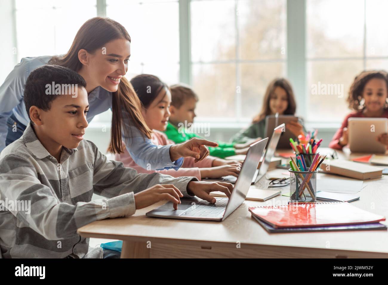 Teacher Teaching Diverse School Kids Using Laptop In Classroom Stock ...
