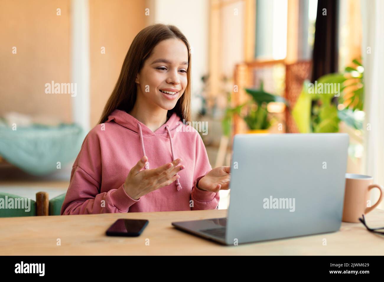 Positive teen girl video calling on laptop and gesturing at webcamera ...