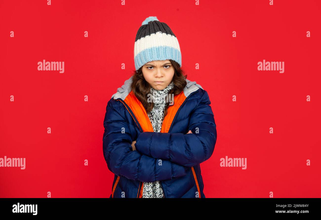 unhappy kid with curly hair in puffer jacket and hat. teen girl on red ...