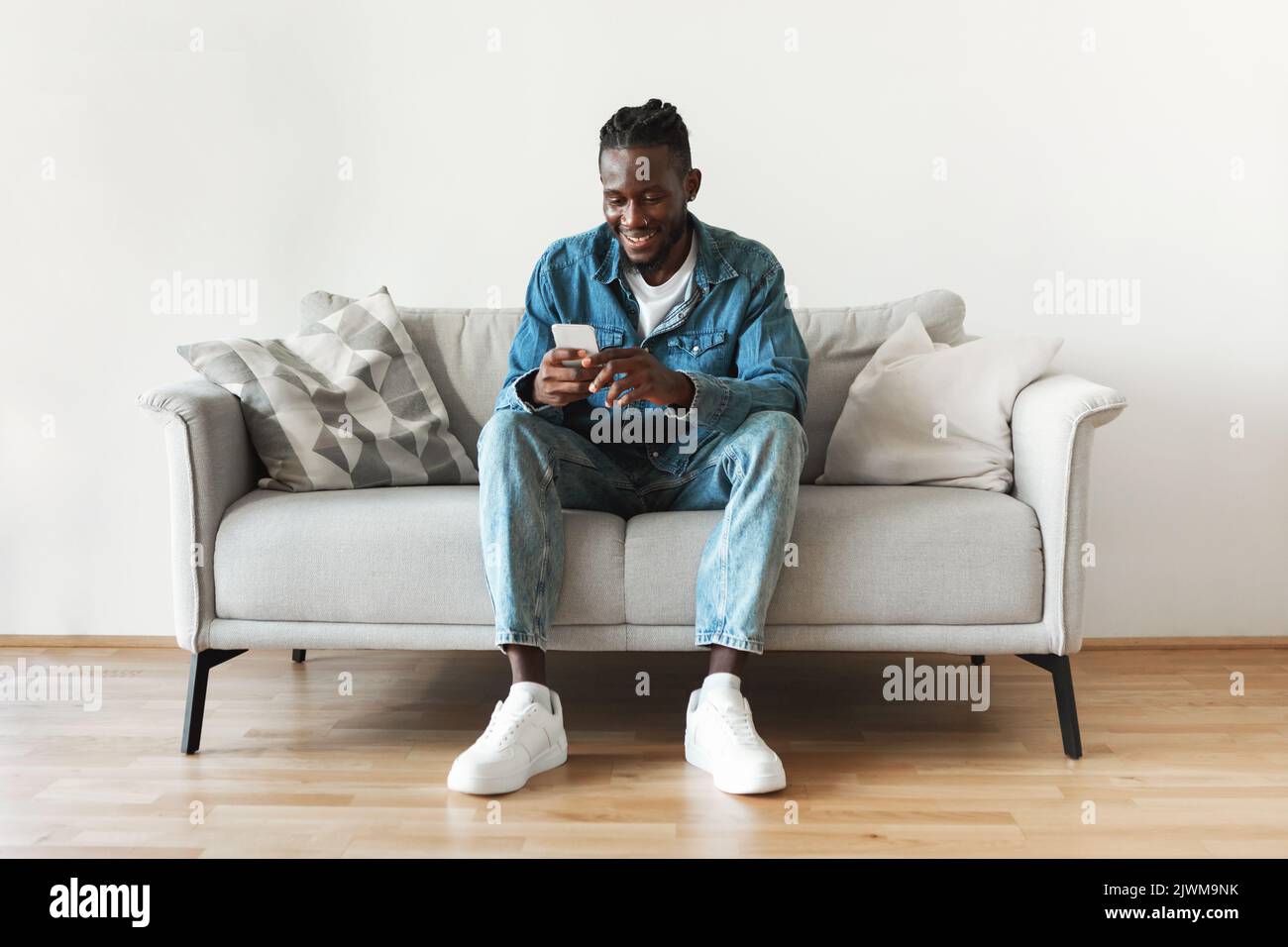 Black Male Using Phone Texting Sitting On Couch At Home Stock Photo - Alamy