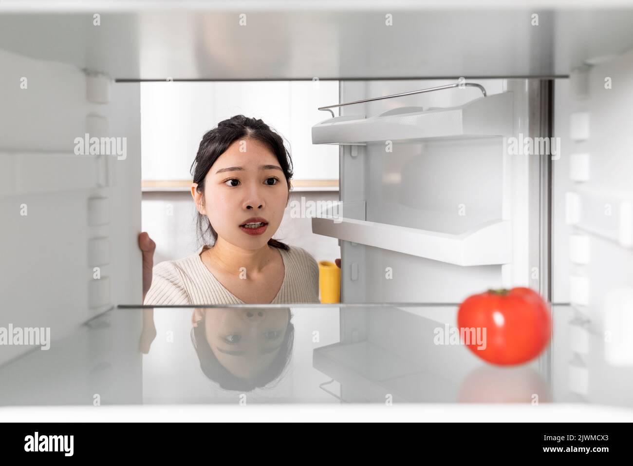 Upset chinese woman looking at lonely tomato in her fridge Stock Photo ...