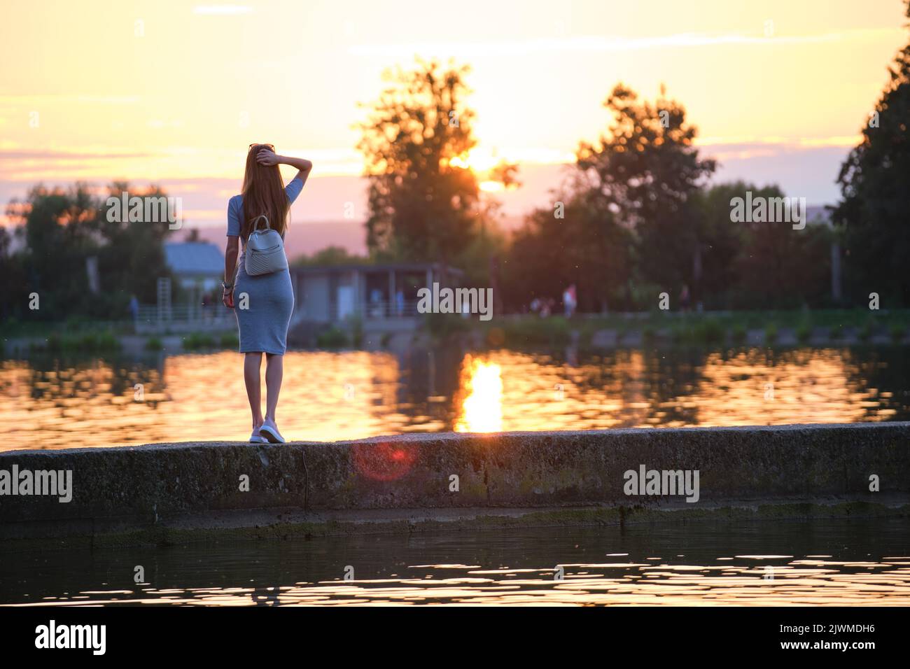 Back view of lonely woman standing on lake side on warm evening ...