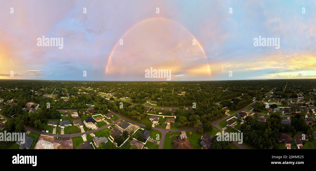 Colorful round rainbow over rural town suburbs against blue evening sky ...