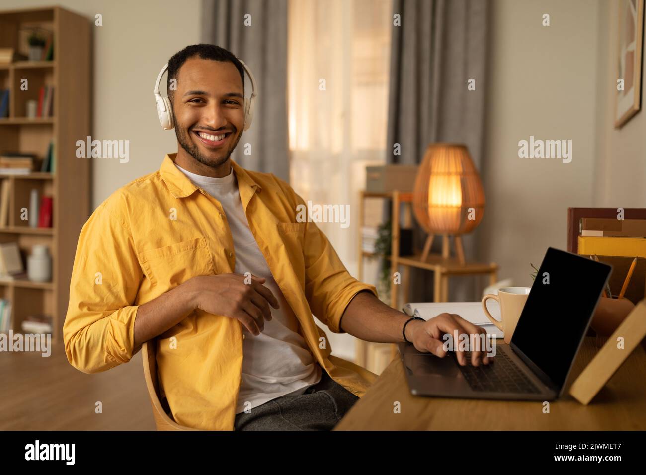 Young happy black man in headphones using laptop pc with mockup ...