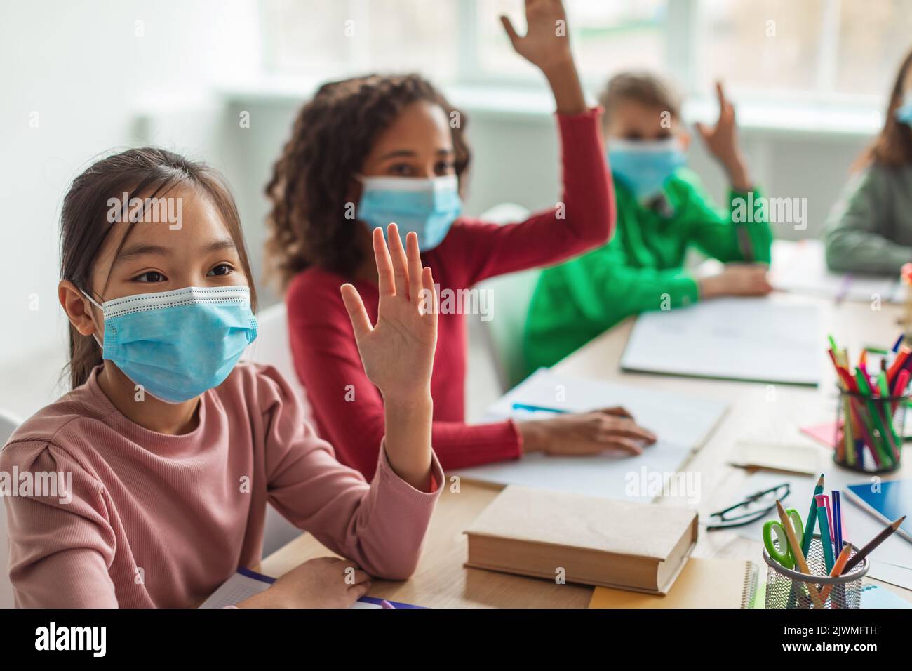 Diverse School Children Wearing Face Masks Raising Arms In Classroom ...